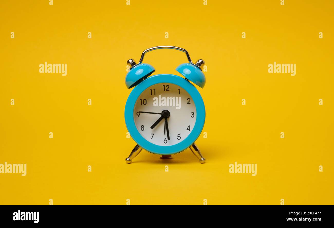 Round alarm clock on a yellow background, half past seven in the ...