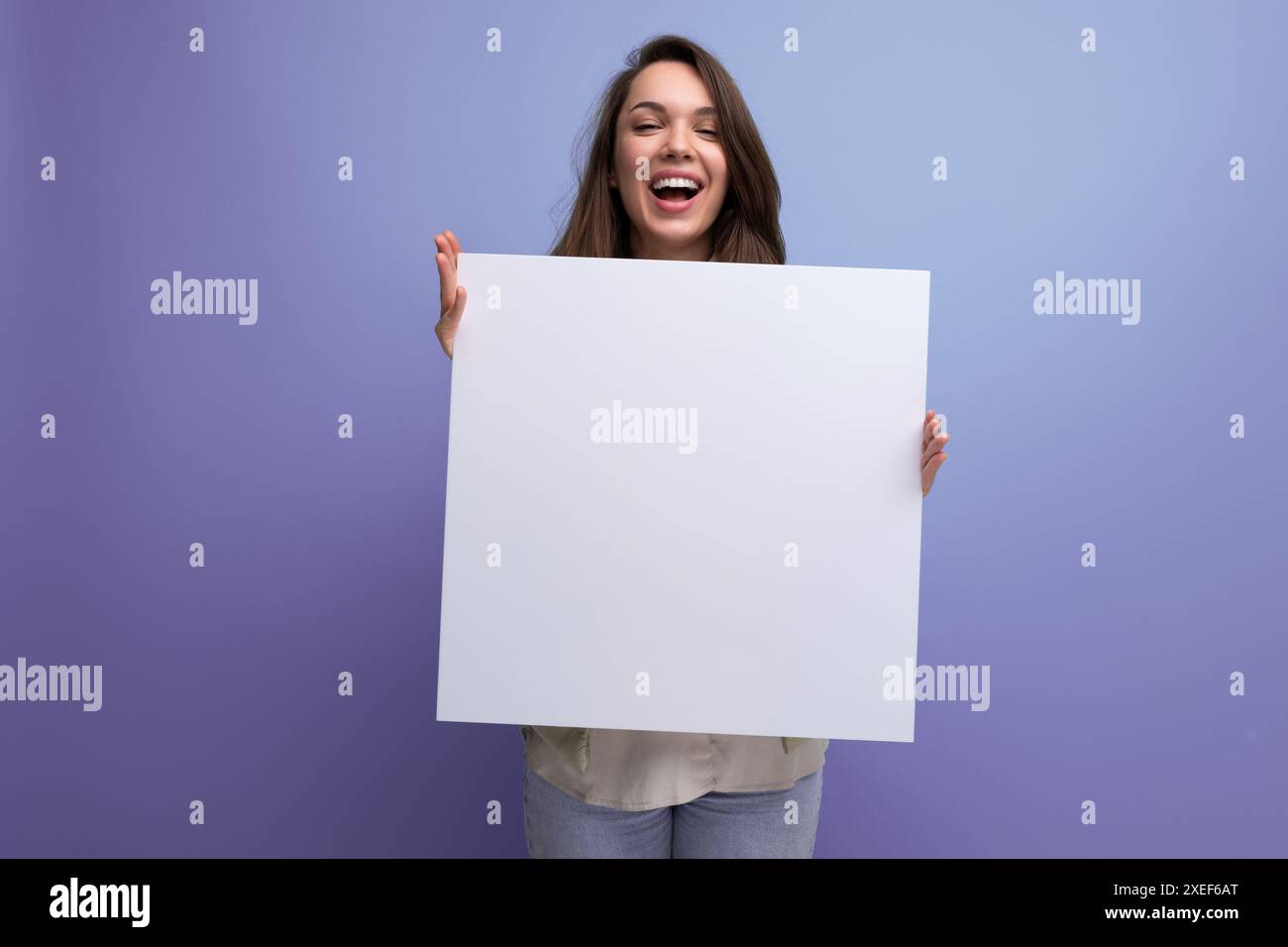 Positive young brunette woman showing advertisement on white sheet ...