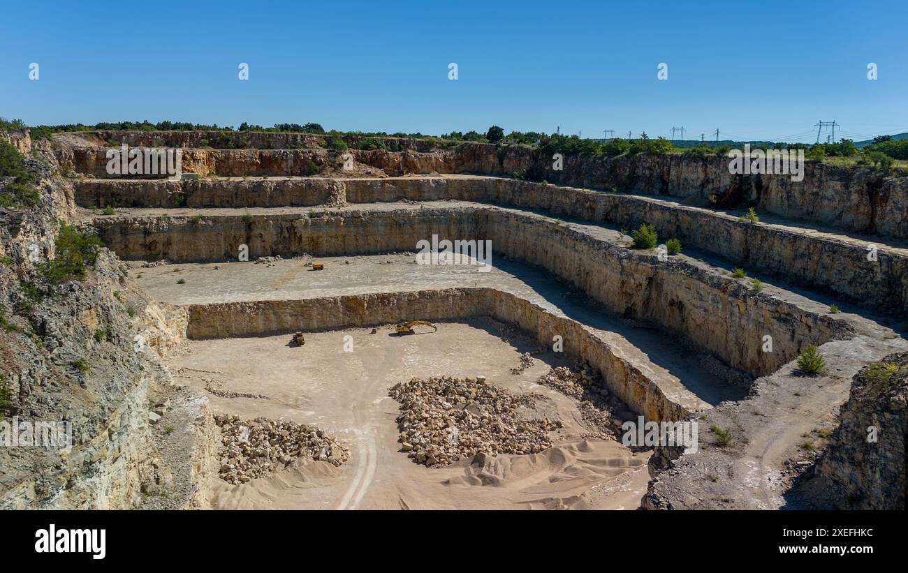 Excavator extracting limestone in an open pit mine surrounded by forest ...