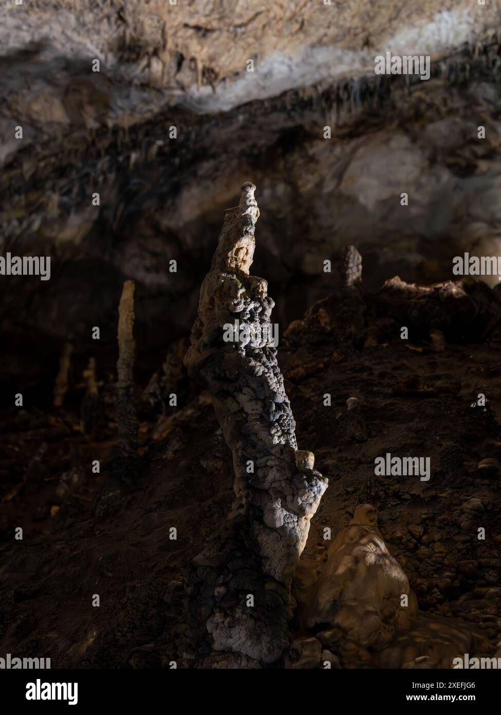 Large stalagmite is growing from the floor of a cave, illuminated by ...