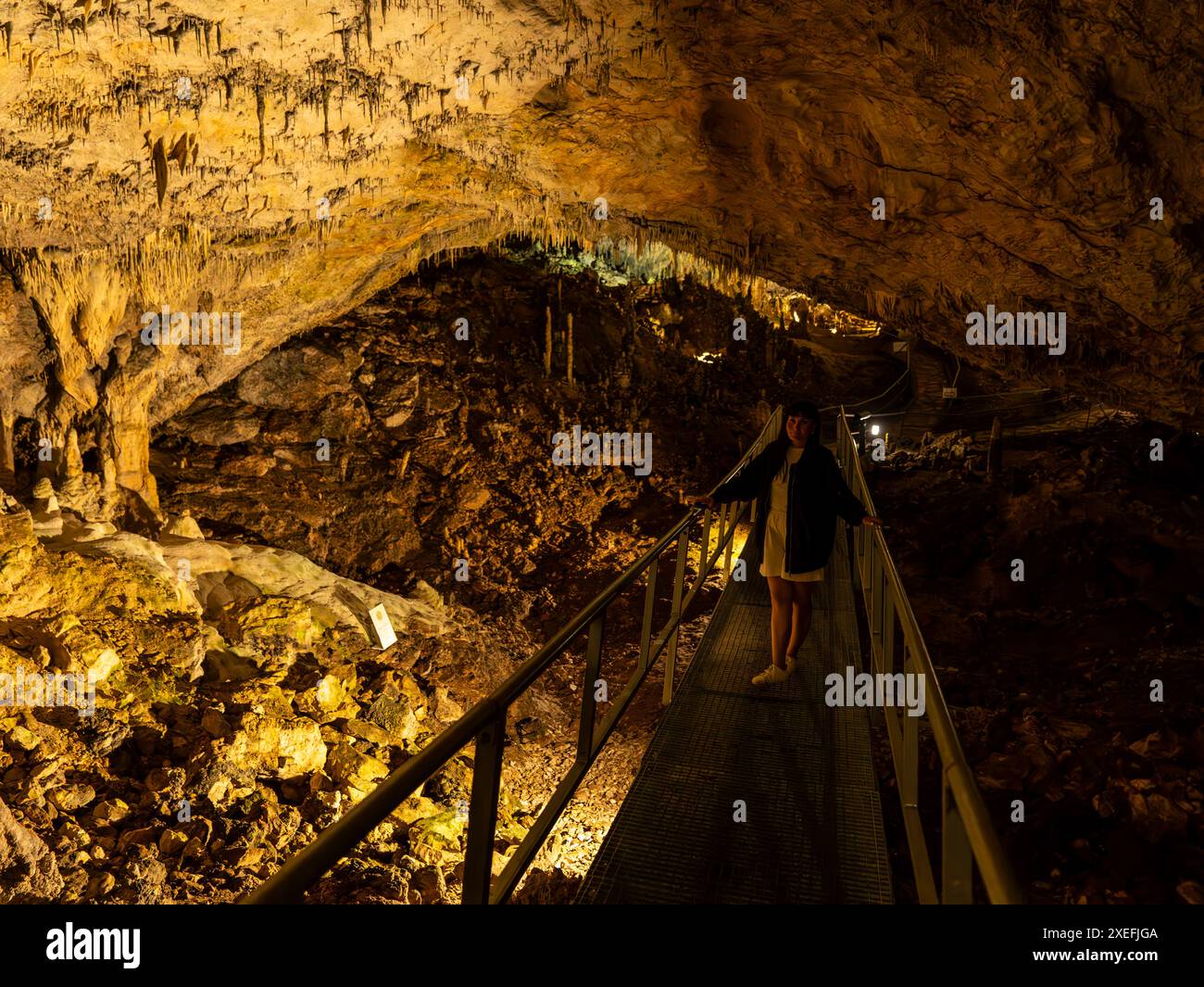 Tourist is walking on a metal pathway inside a large cave with ...