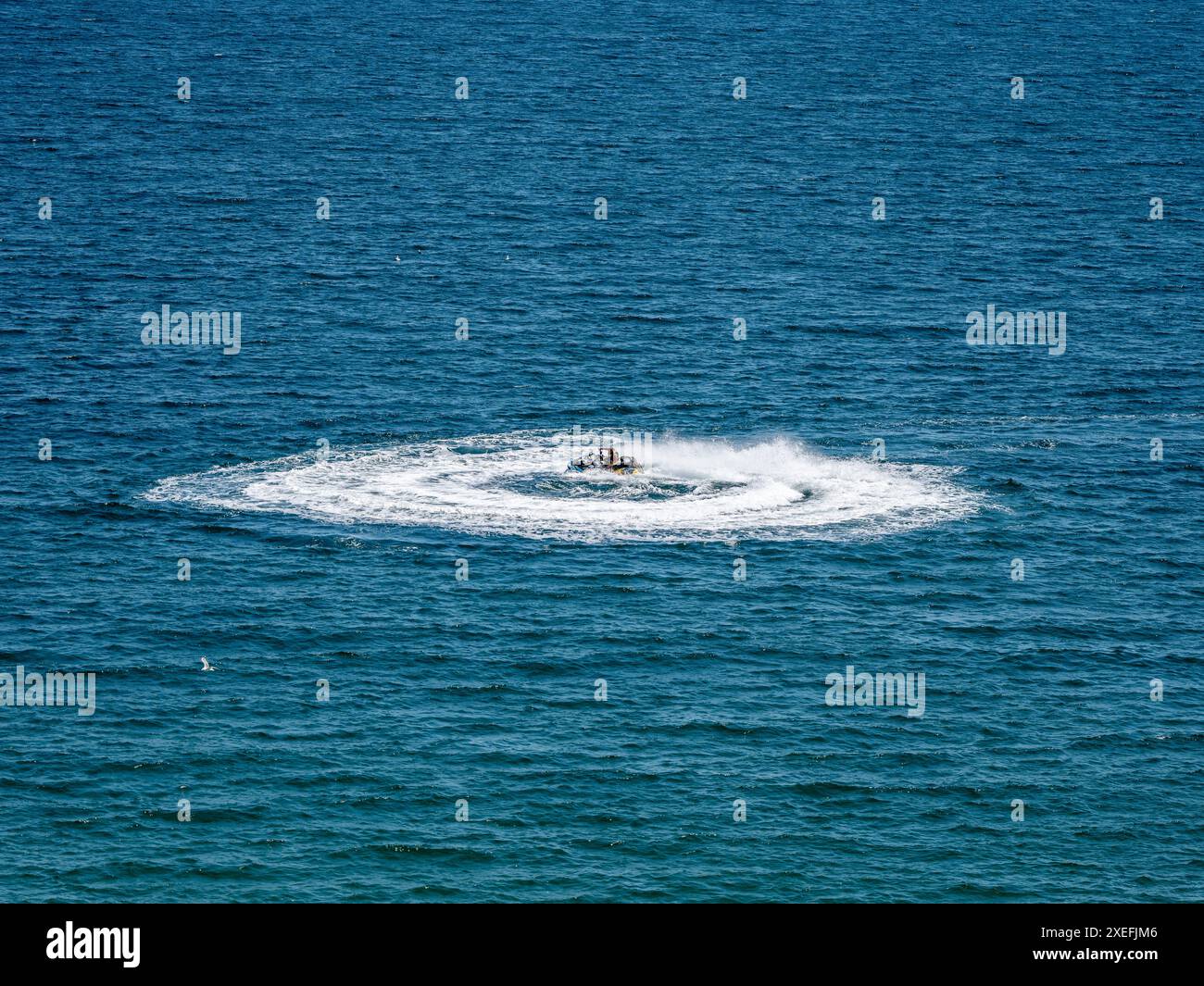 Man on a jet ski is leaving a circular wave trail on the surface of the ...