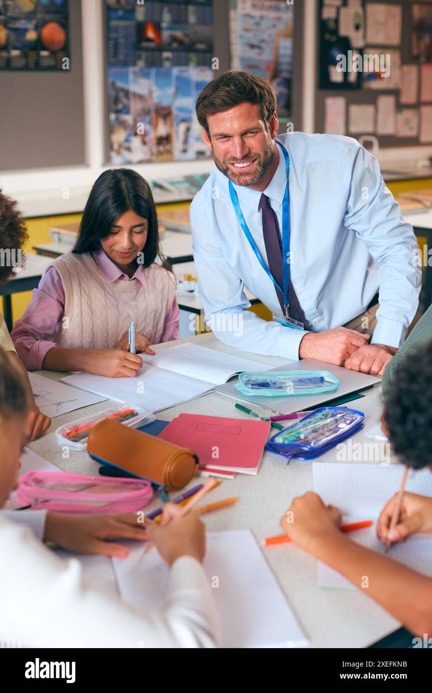 Male Secondary Or High School Teacher Sitting At Table Working With ...