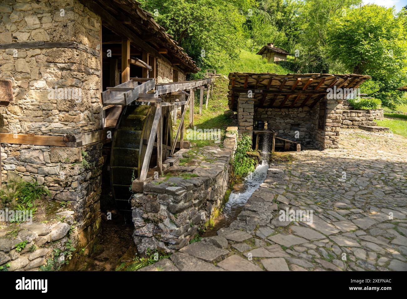 Traditional watermill building with wooden water wheel turning on small ...
