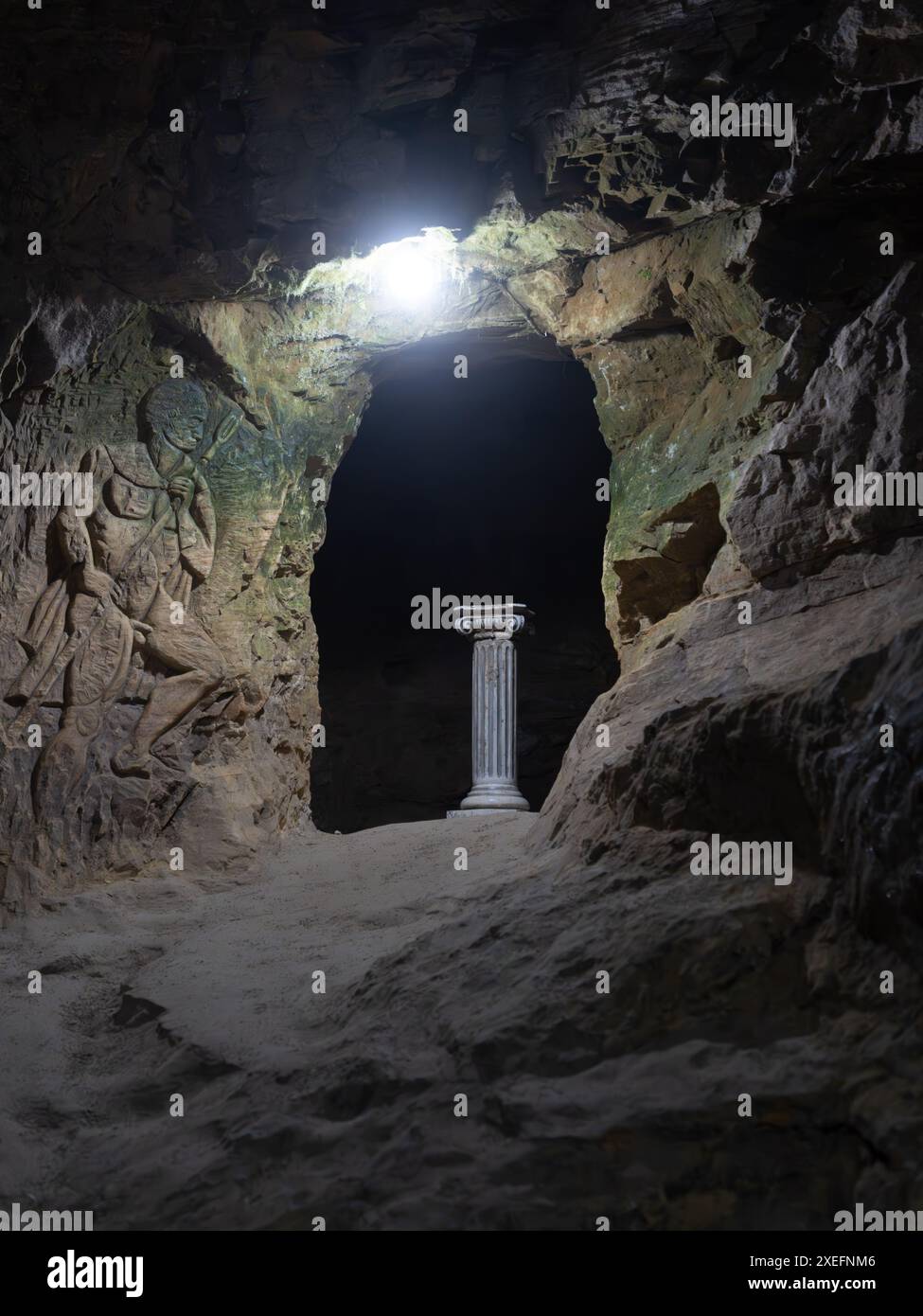 Light illuminating ancient carvings on cave wall with column in the ...