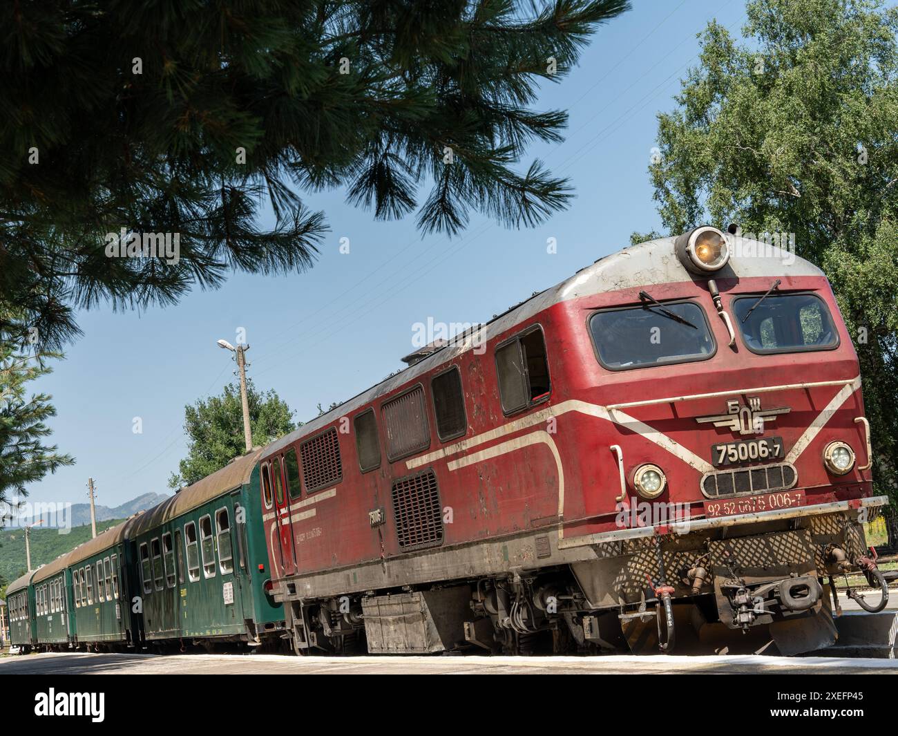 Old red train engine pulling green passenger carriages at a station ...