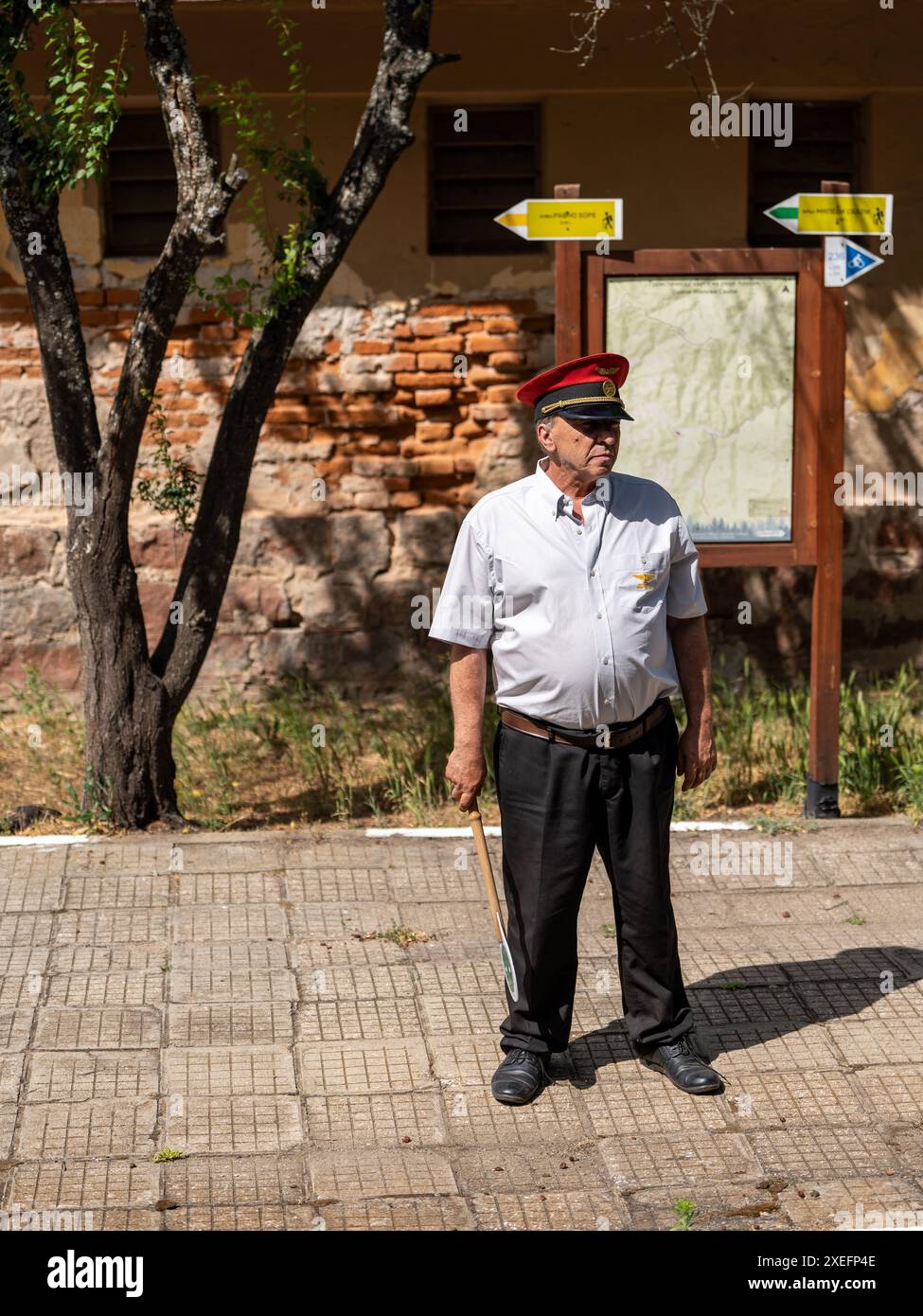 Old park ranger is standing outside on a stone patio holding a stick in ...