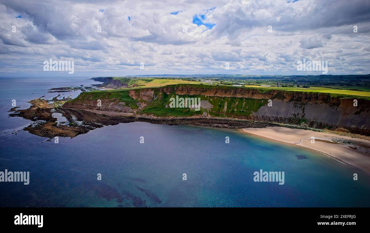 Aerial view of a coastal cliff with green fields on top, rocky ...