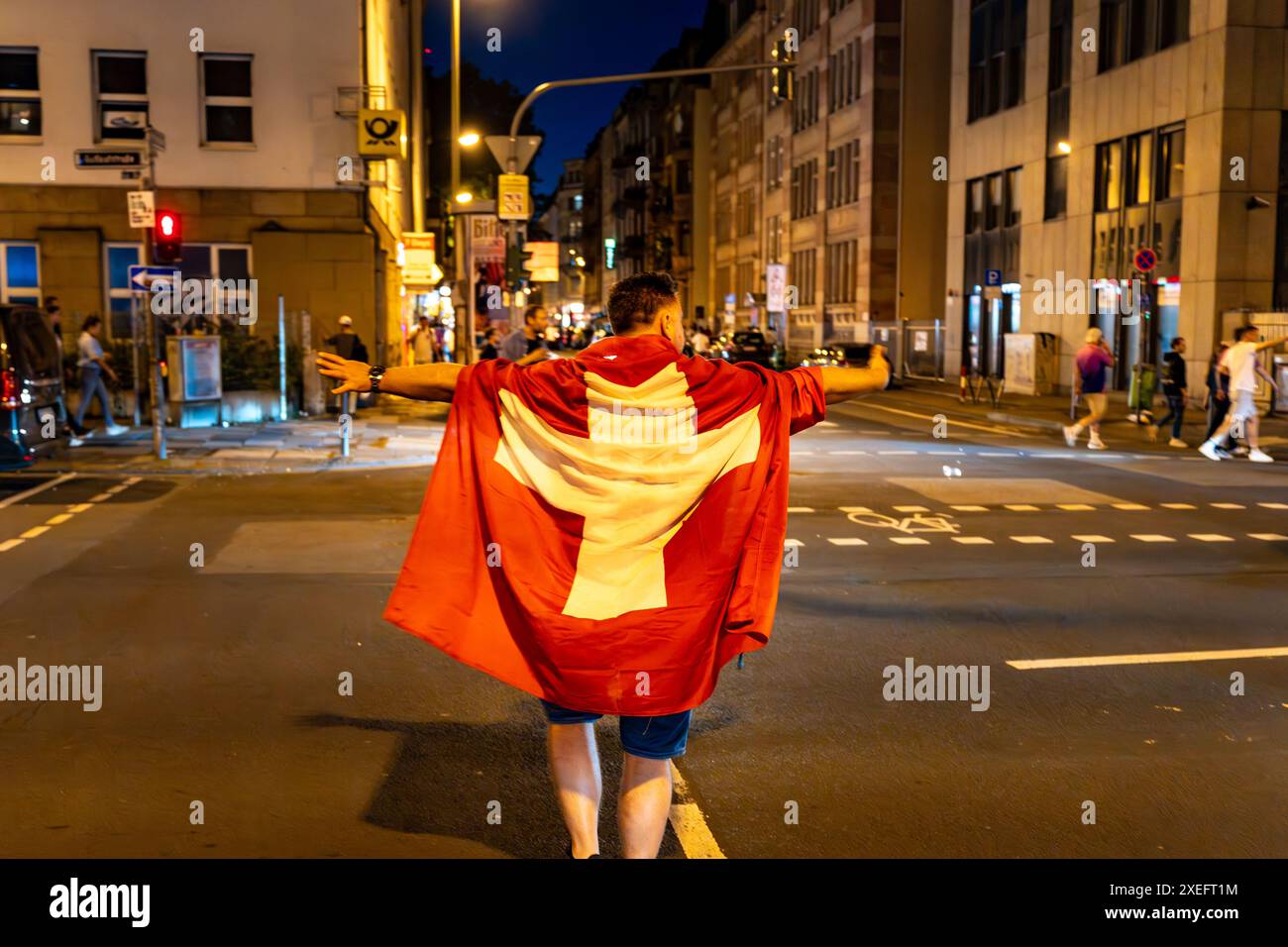 A man with a Swiss flag draped over his shoulders standing in a city ...