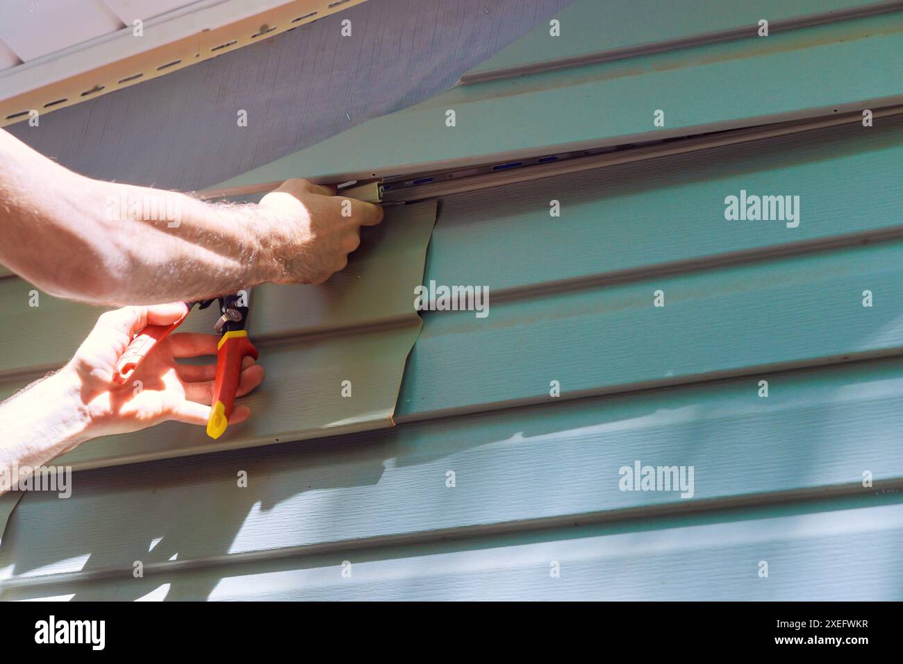 Worker installing vinyl plastic siding panels on wall facade of new ...