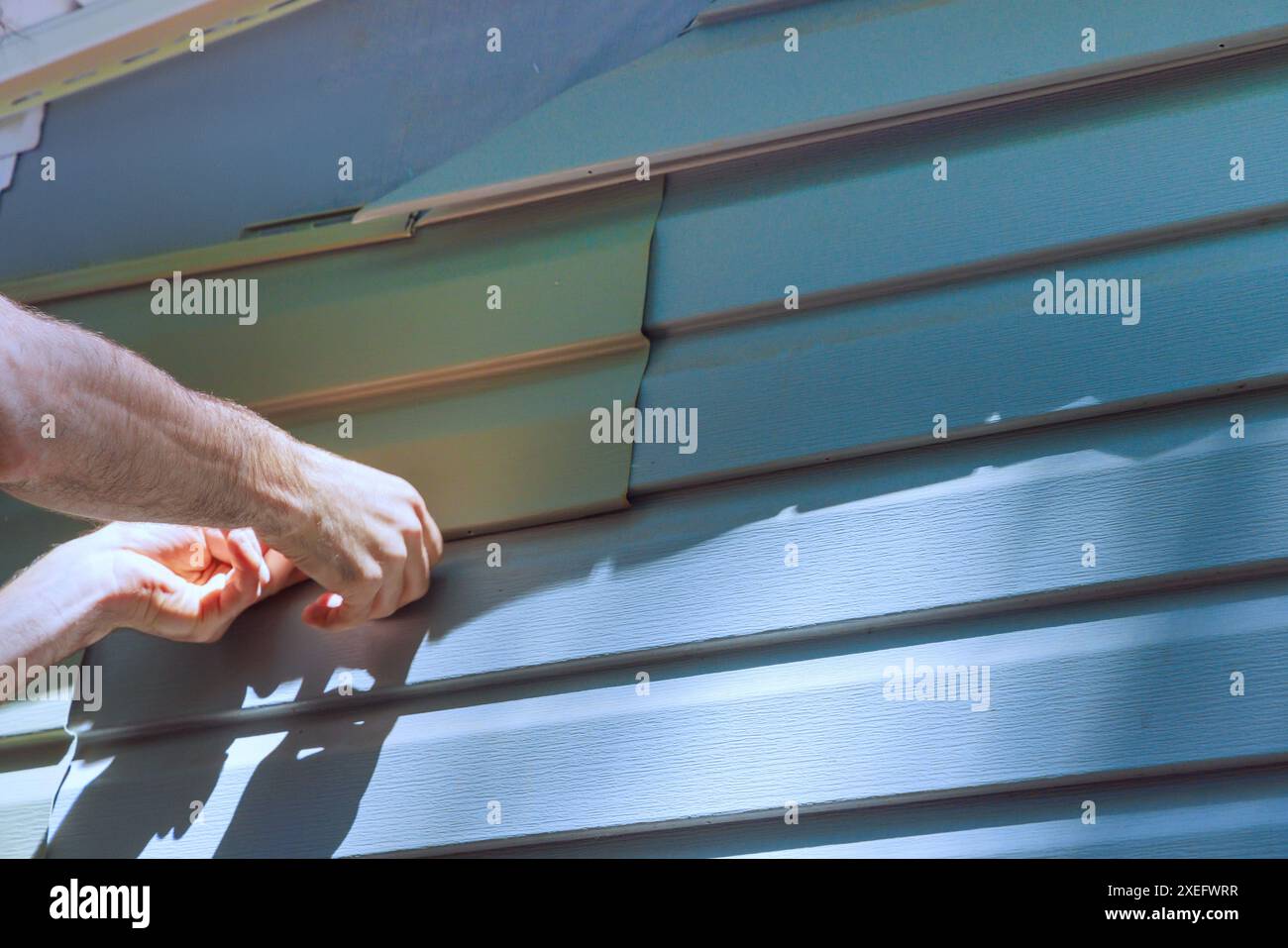 Workers install vinyl plastic siding panels on wall facade of new home ...