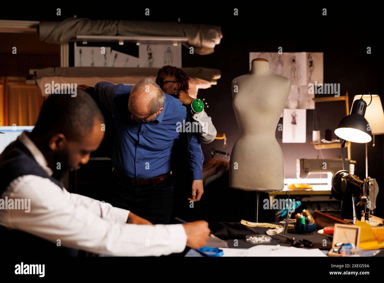 Needleworker helping senior client try on unfinished suit garment while ...