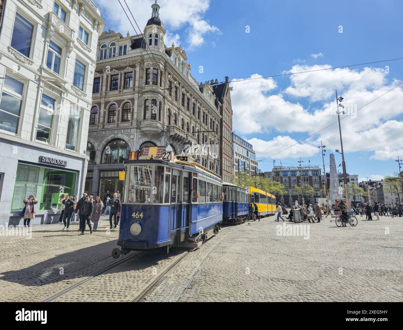 A vibrant blue and yellow trolley travels along a bustling city street ...