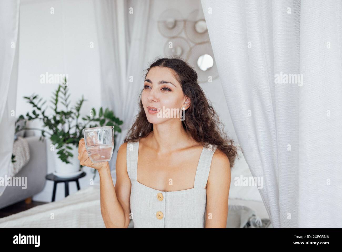 A charming curly-haired brunette in a linen sundress holds a ...