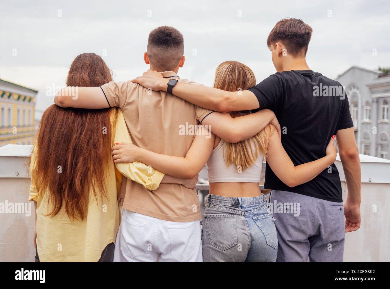 Four teenagers hug and stand with their backs on the roof of the house ...