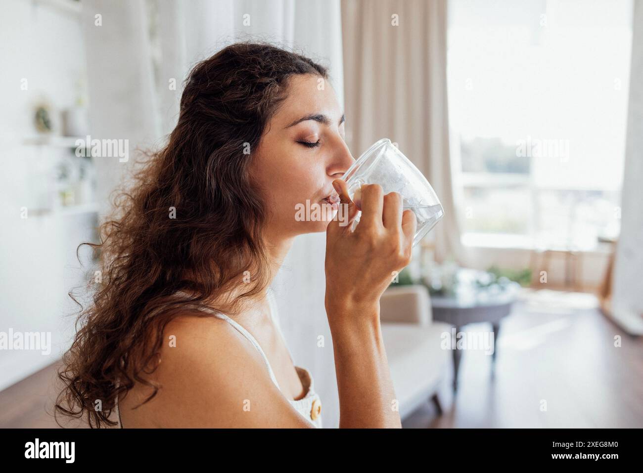 A charming curly-haired brunette in a linen sundress holds a ...