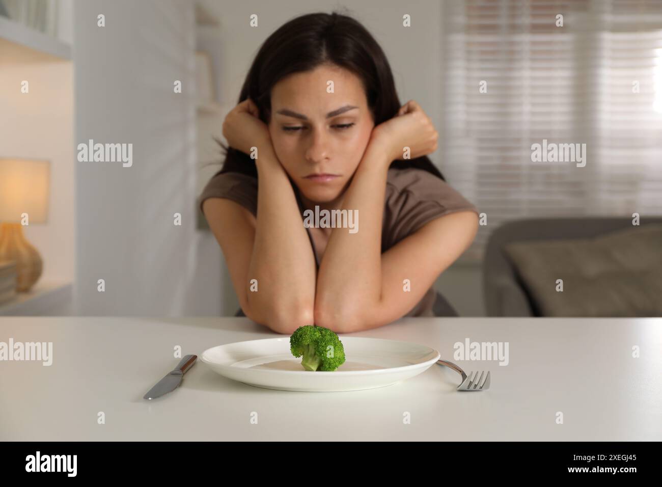 Eating disorder. Sad woman at white table with cutlery, broccoli and ...
