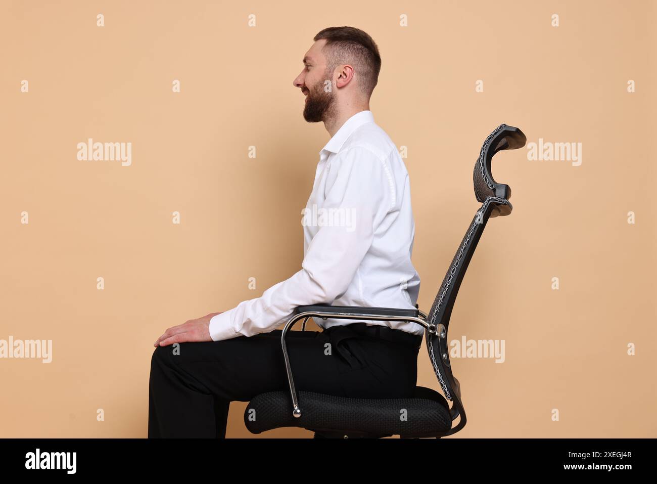 Man with good posture sitting on chair against pale orange background ...