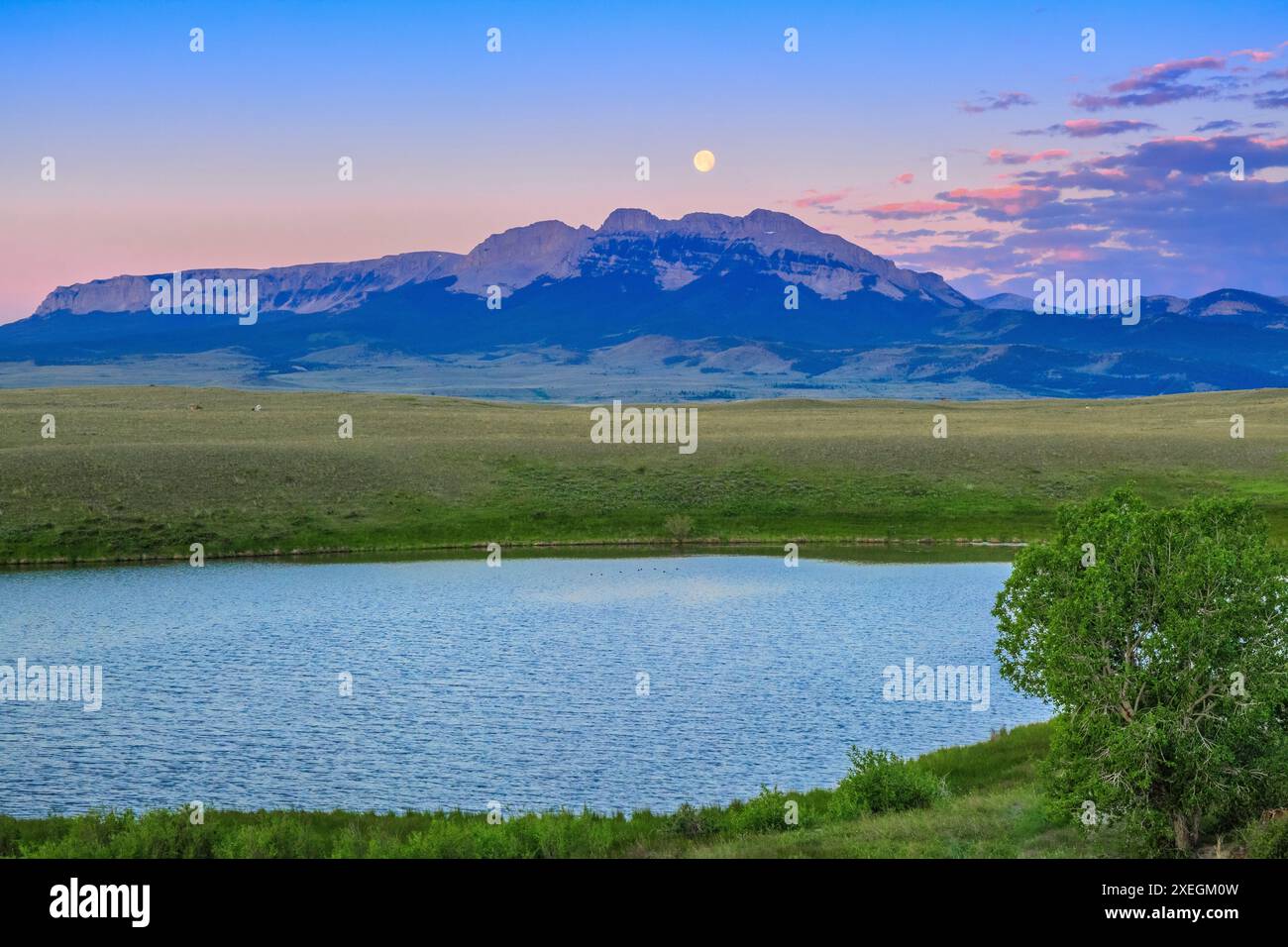 full moon setting over sawtooth ridge and a prairie pond near choteau ...