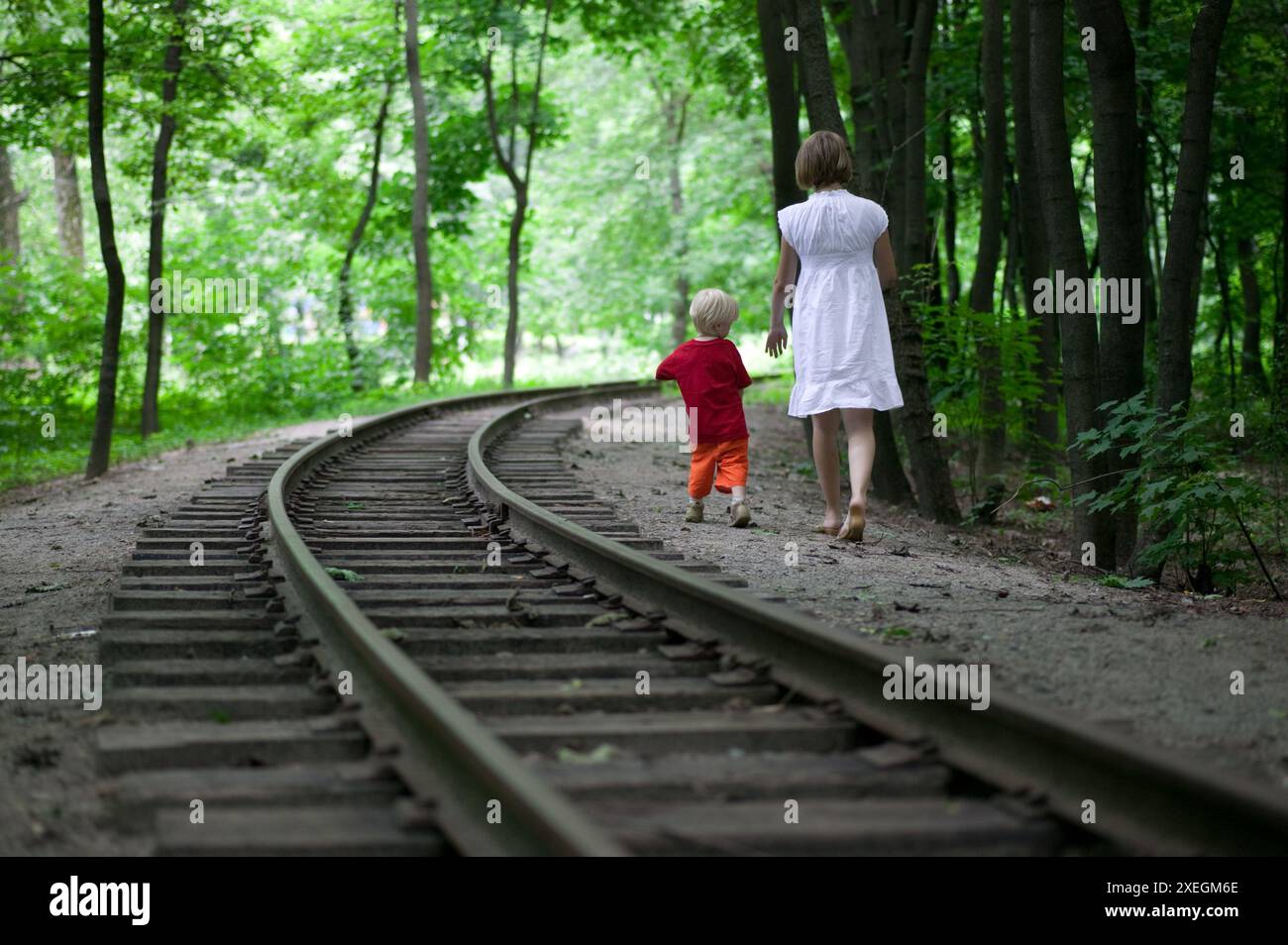 A woman and a child walk on a set of railroad tracks that curve through ...