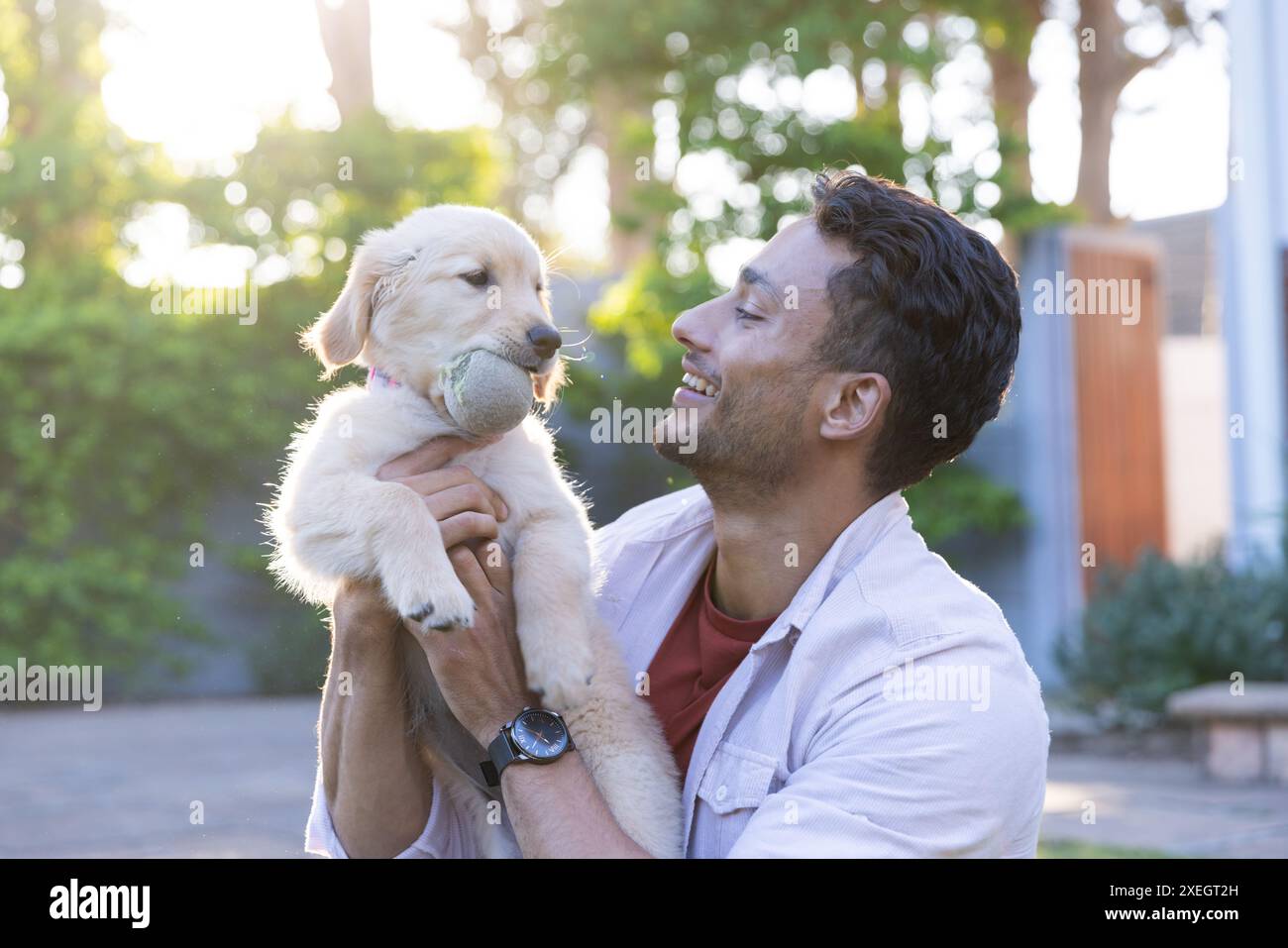 Man holding puppy with tennis ball, smiling outdoors in backyard Stock ...