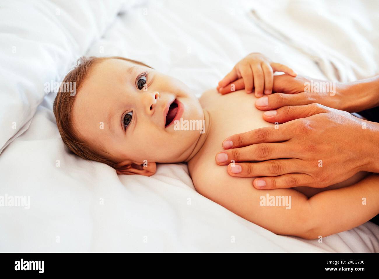 A cute smiling baby and his mom hands. A mother touches her little son ...