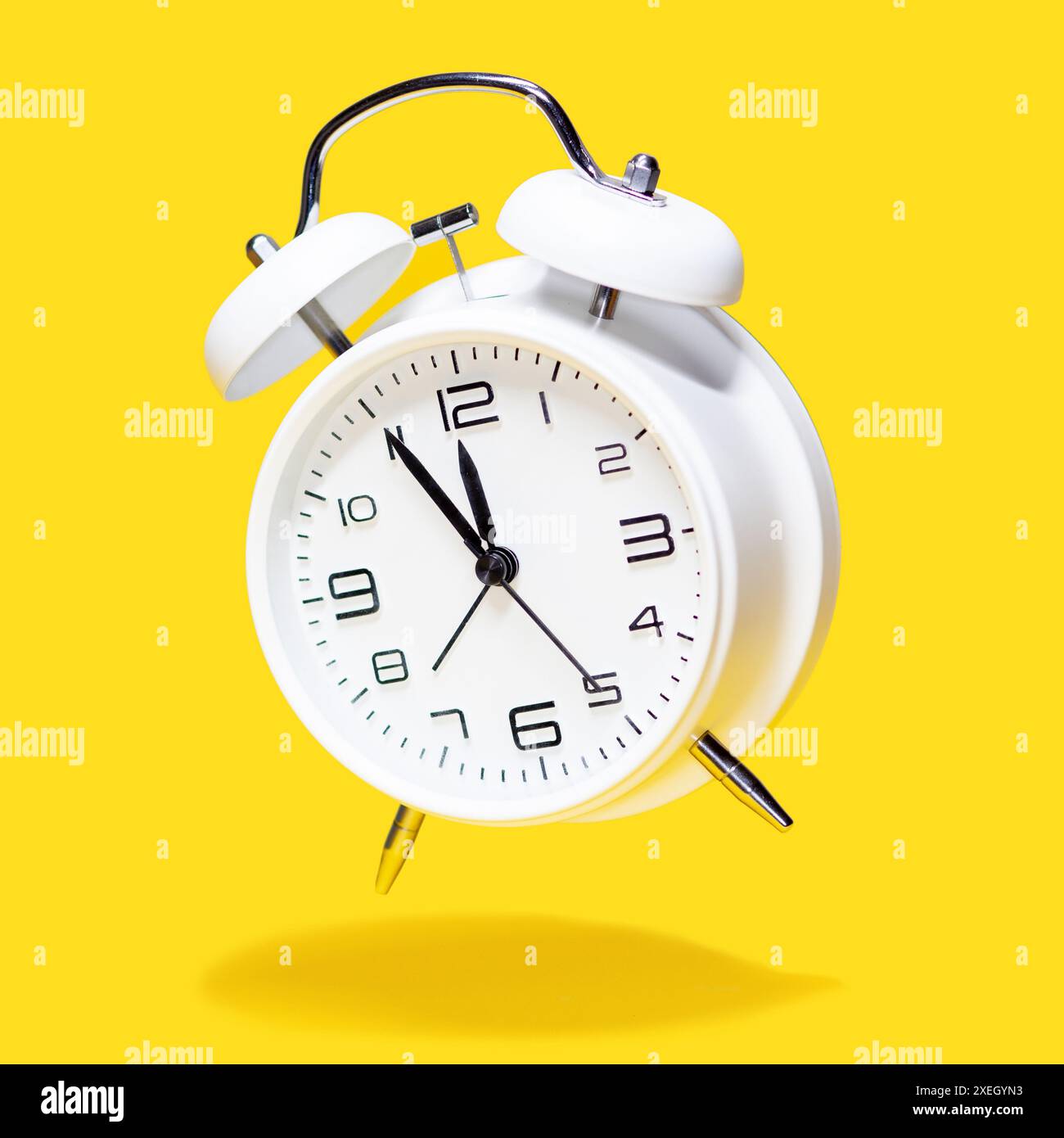 White bell alarm clock hovering over yellow background. 5 to 12 clock ...