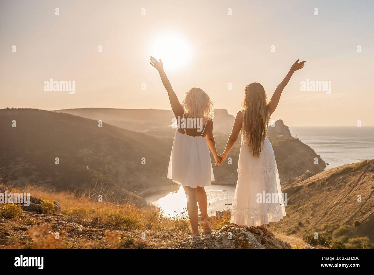 Two women are standing on a hill overlooking the ocean. They are ...
