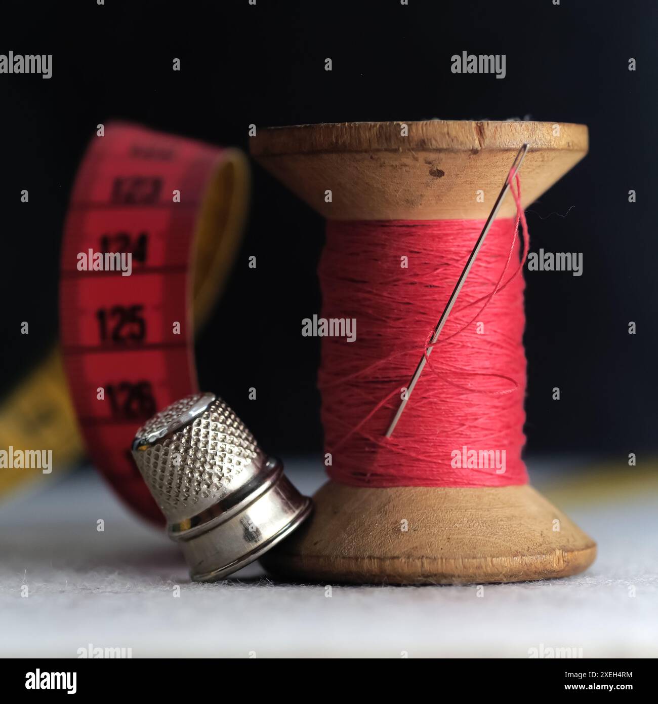 Wooden vintage spool of red thread, needle, metal thimble on abstract ...