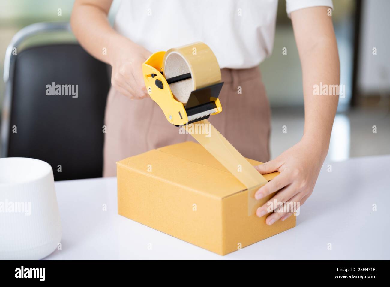 Female post mail storage worker holding tape dispenser sealing shipping ...