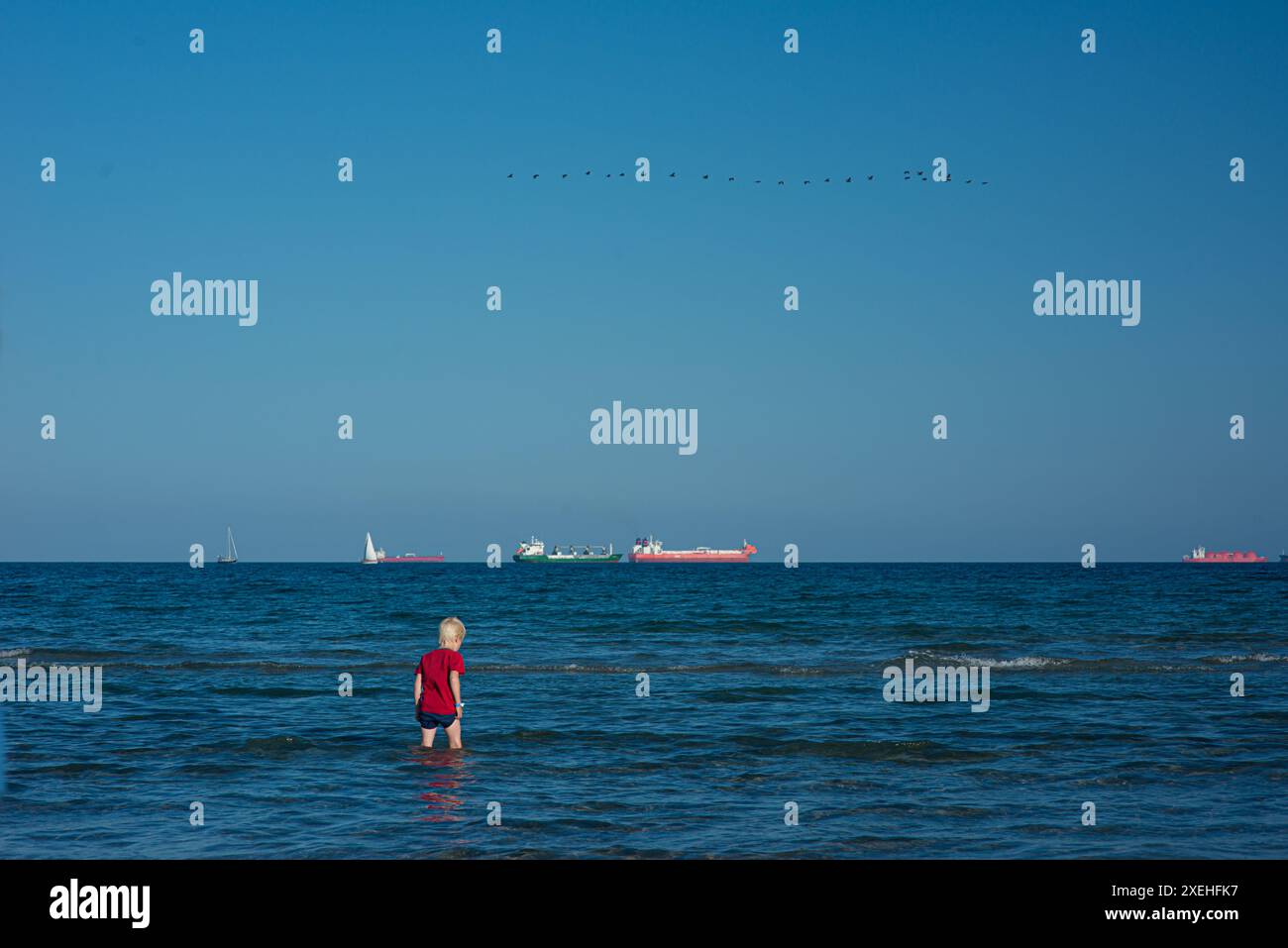 Kid wading in the sea with tanker ships on the horizon Stock Photo - Alamy