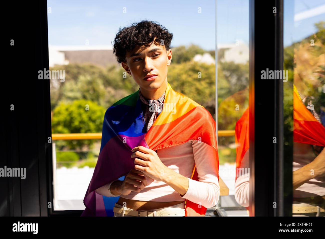 Wearing rainbow flag, transgender woman standing by window, embracing ...