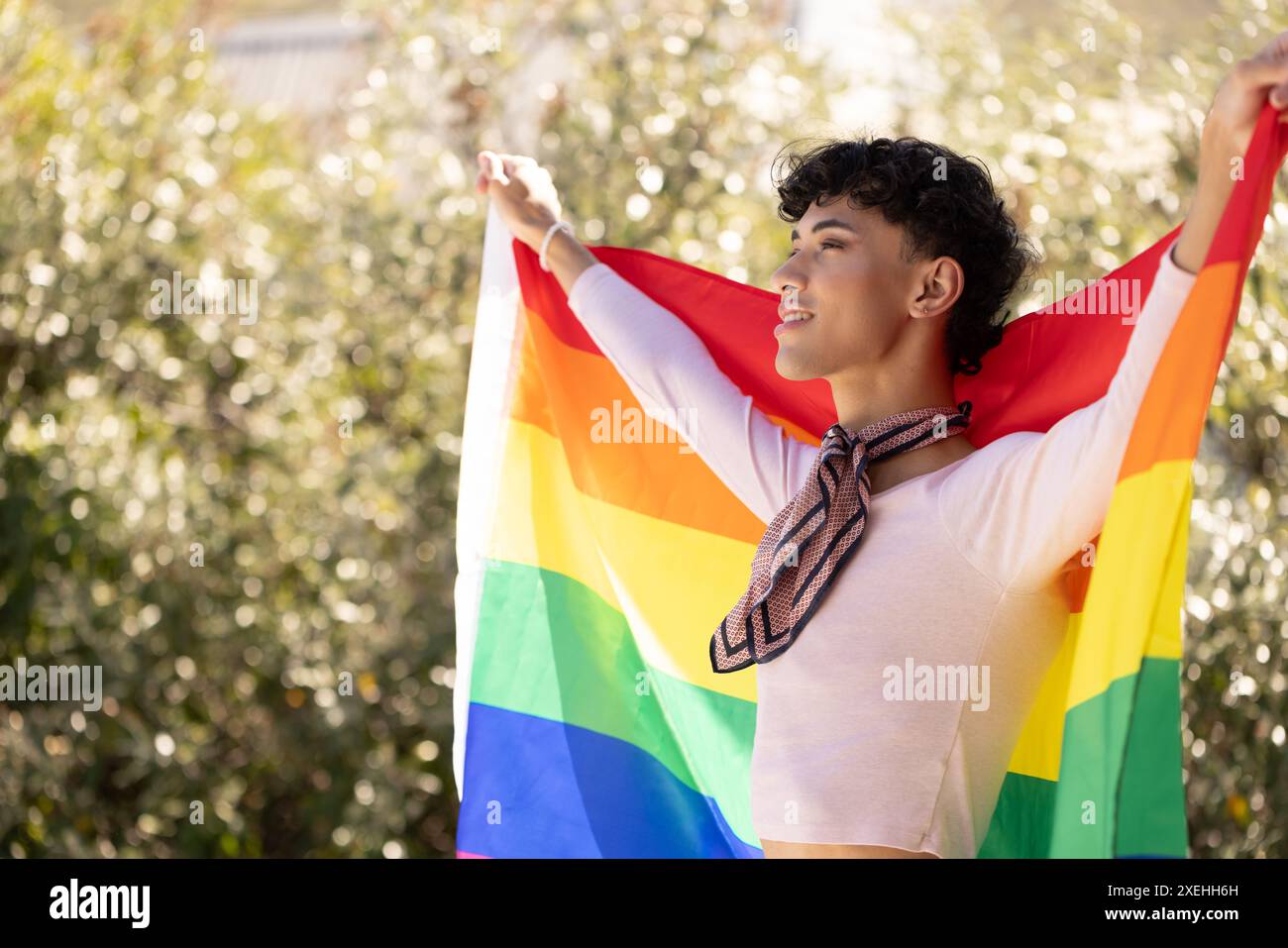 Holding rainbow flag, young man celebrating LGBTQ+ pride outside with ...