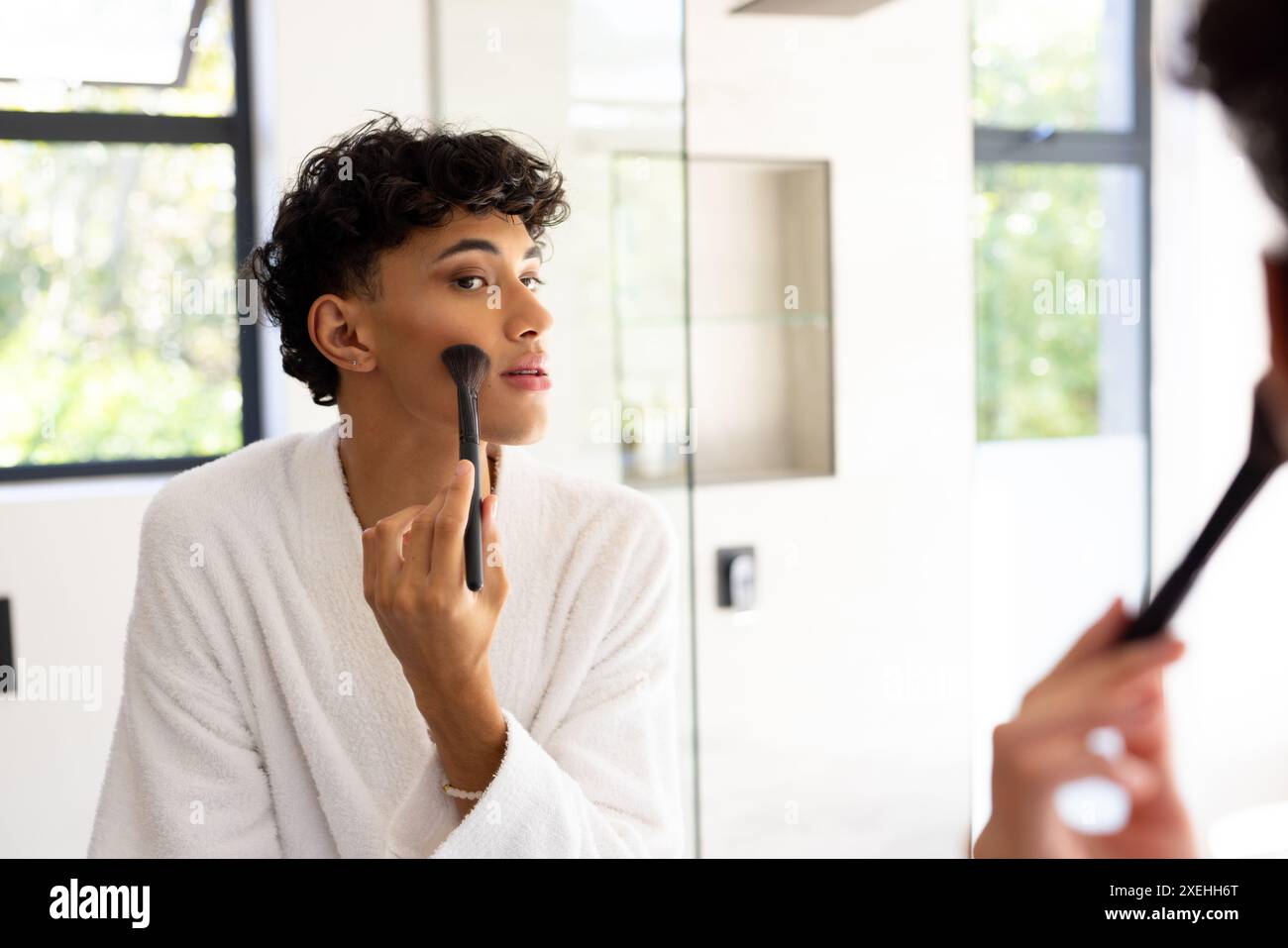 Applying makeup, transgender woman in bathrobe looking in mirror at ...