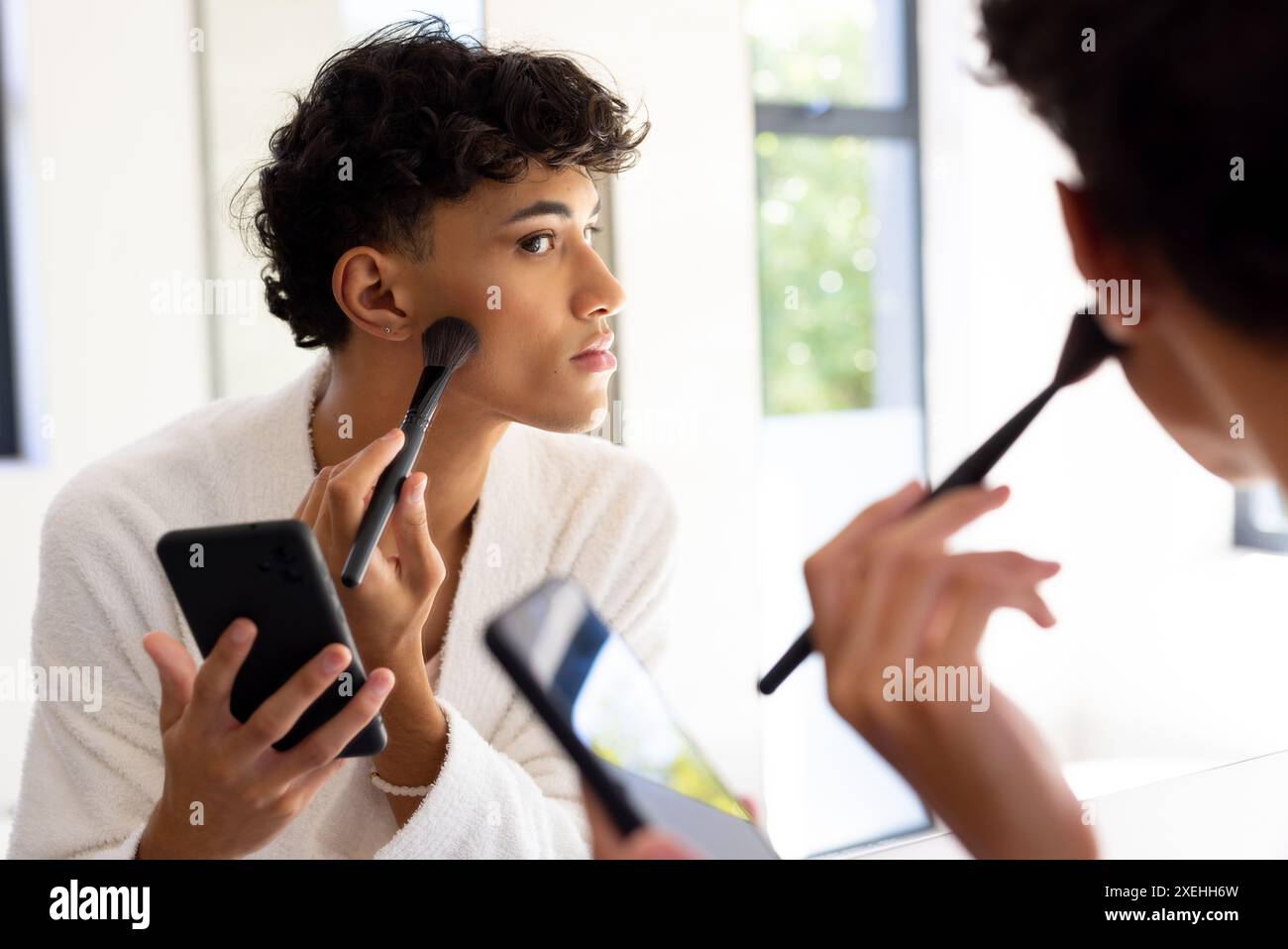 Applying makeup, transgender woman using smartphone while looking in ...