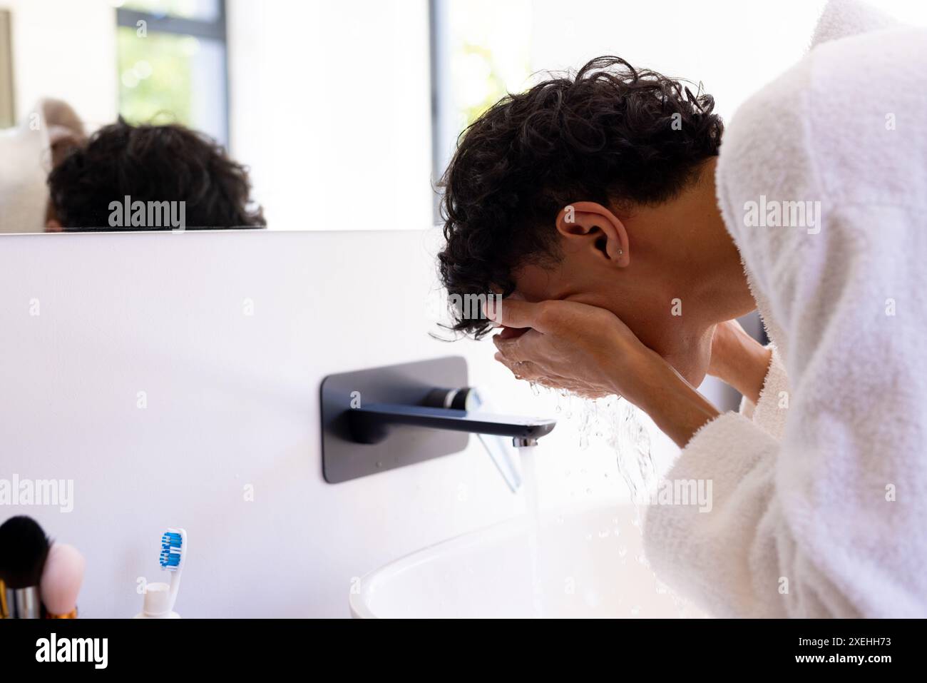Washing face in bathroom, young man wearing white robe in front of mirror Stock Photo - Alamy