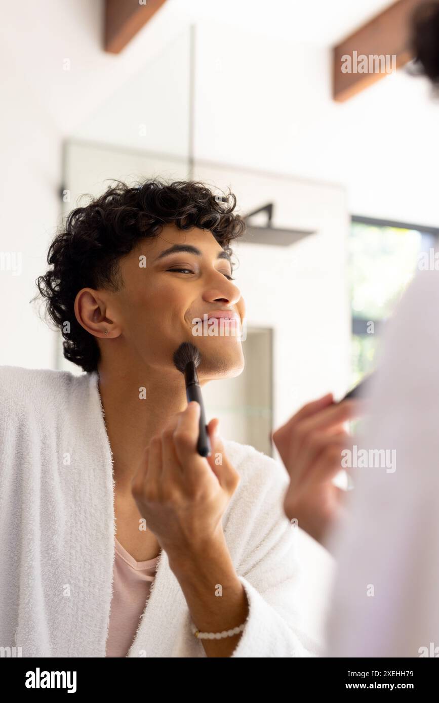 Applying makeup, transgender woman smiling in front of bathroom mirror ...