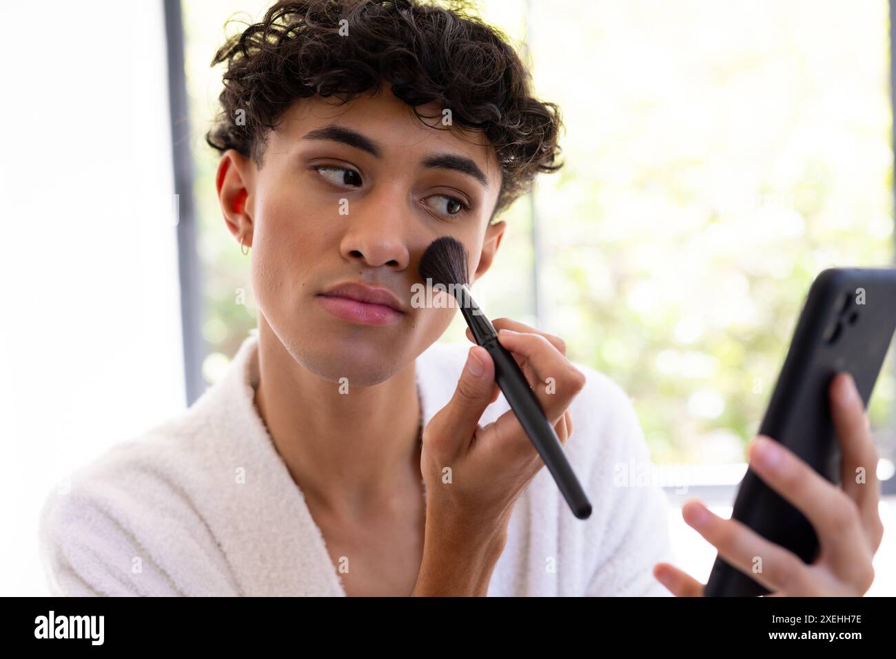 Applying makeup, transgender woman using smartphone as mirror at home ...