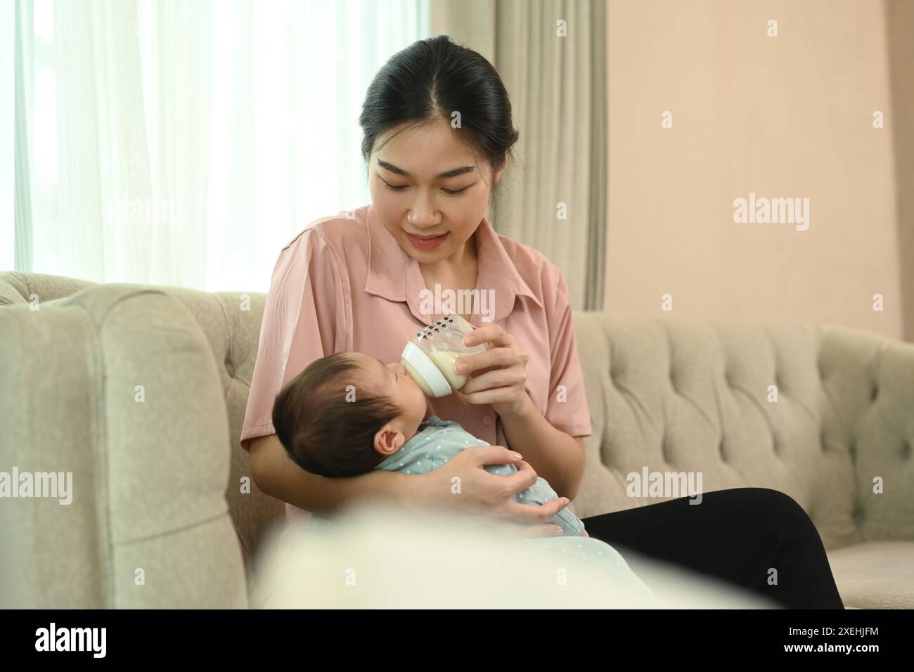 Portrait of loving Asian mother feeding her newborn baby from a bottle. Motherhood and Love ...