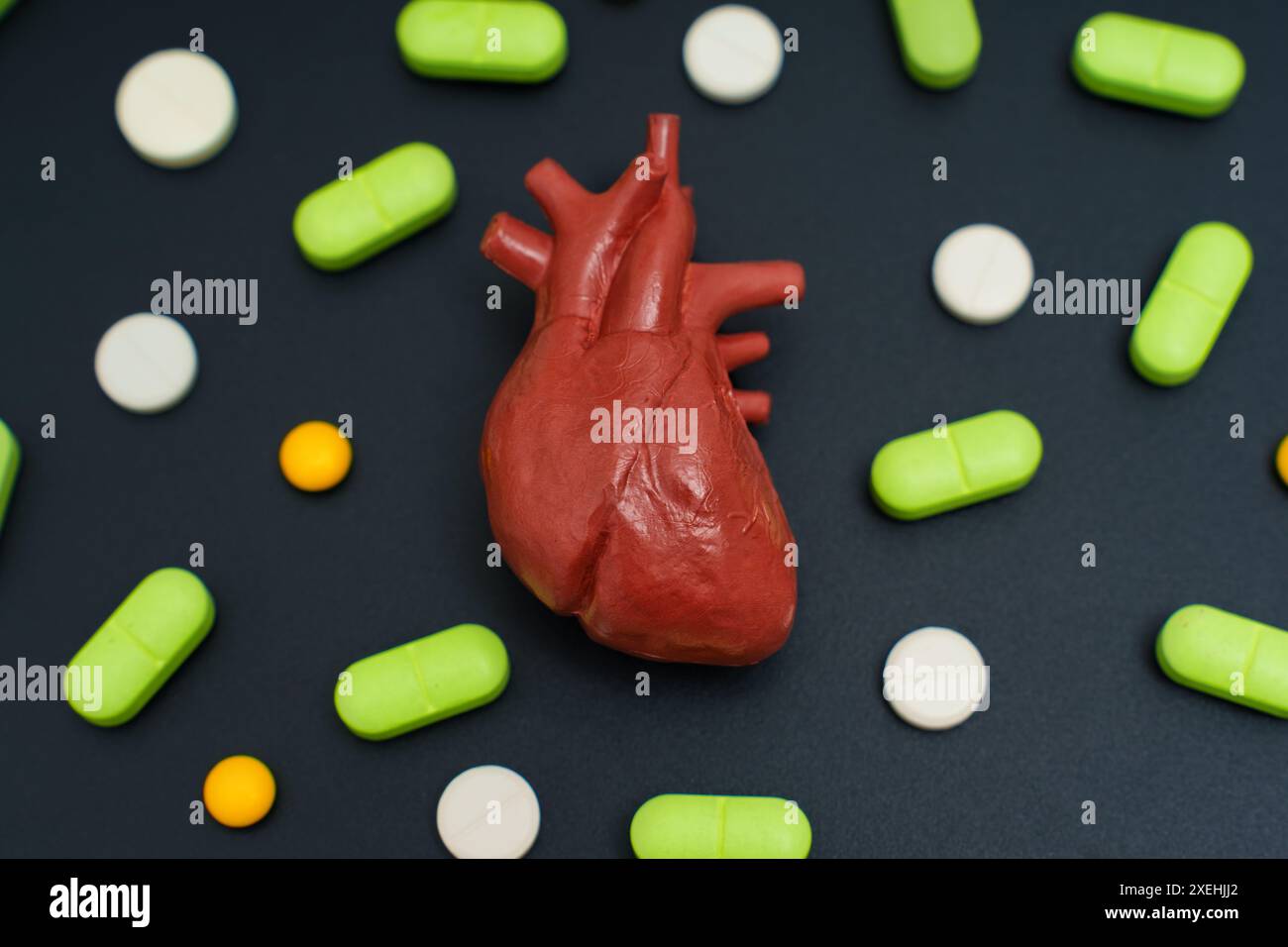 Anatomical model of a human heart surrounded by various pills on a ...
