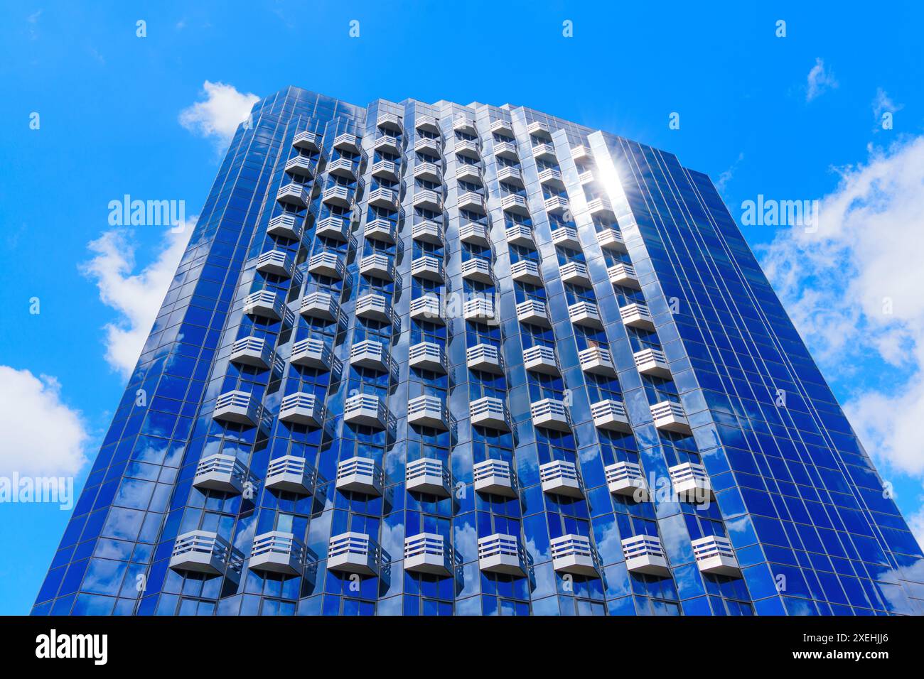 Upward view of a contemporary glass skyscraper under a bright sky. The ...