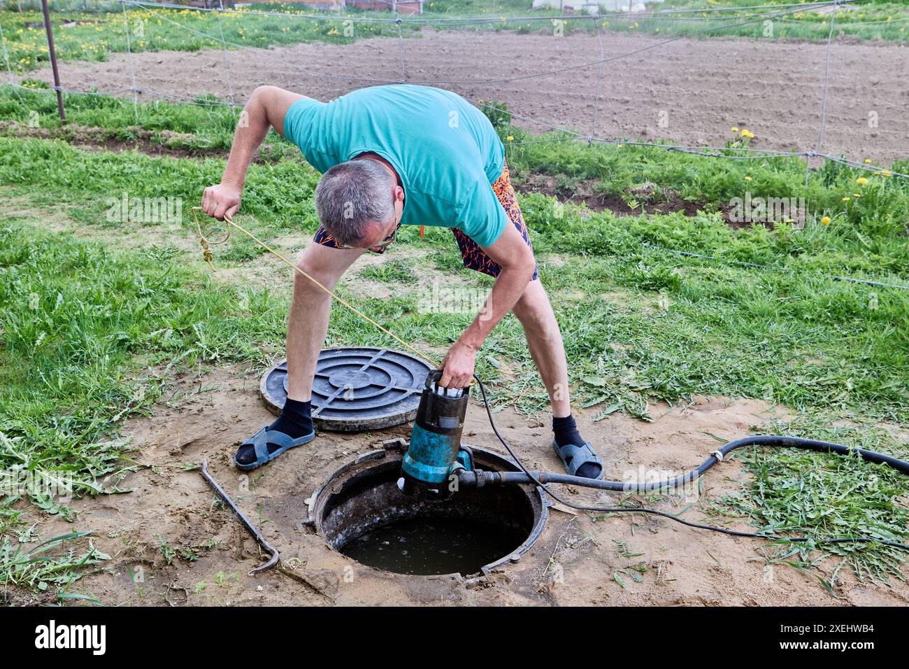Man lowers high pressure submersible drainage pump into septic tank to ...