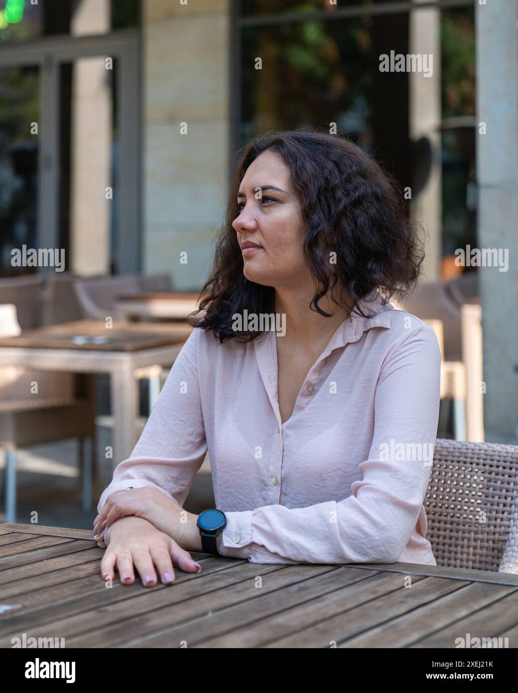 A girl with dark hair sits in a street cafe and looks thoughtfully into ...