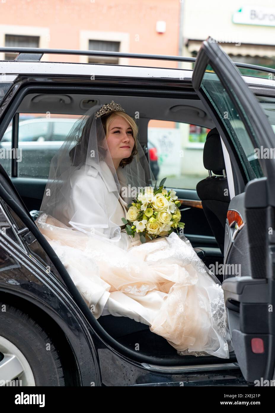A beautiful, young bride with a large bouquet of white roses sits in a ...