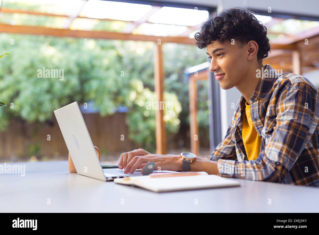 Using laptop, teenage boy working from home at desk with notepad, copy ...