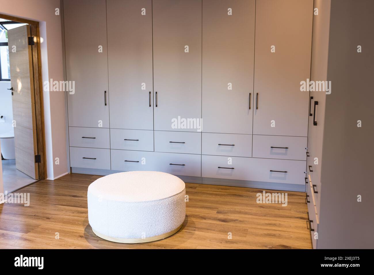 Modern walk-in closet with built-in cabinets and round ottoman in home ...