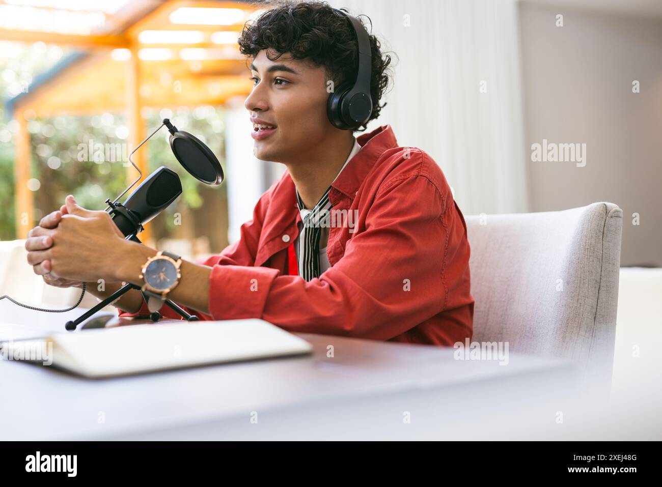 Recording podcast, young man in red shirt speaking into microphone with ...