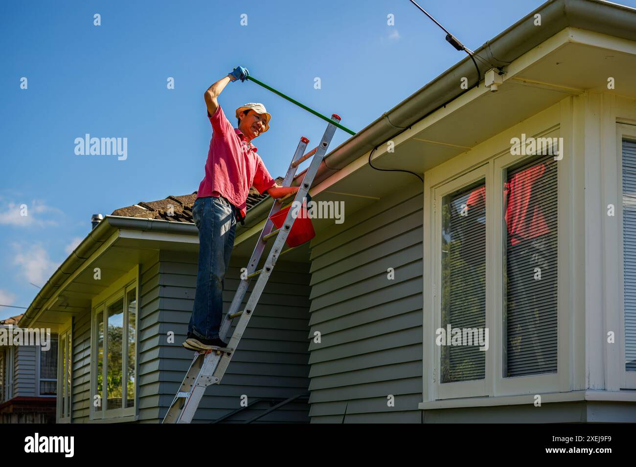 Man standing on the ladder and cleaning gutter with a gutter cleaning ...