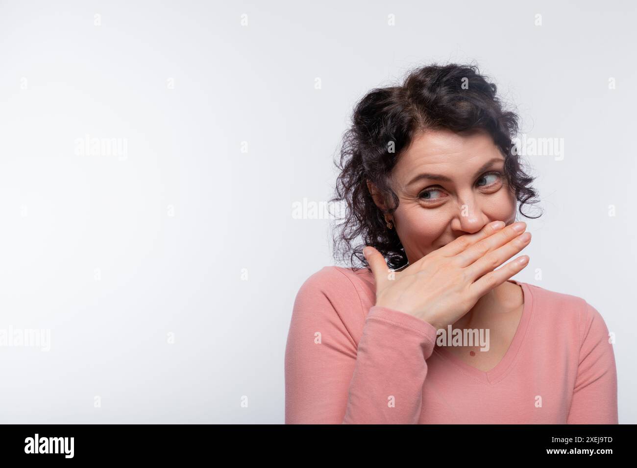 Brunette with curly hair in a pink blouse is embarrassed and hides her ...