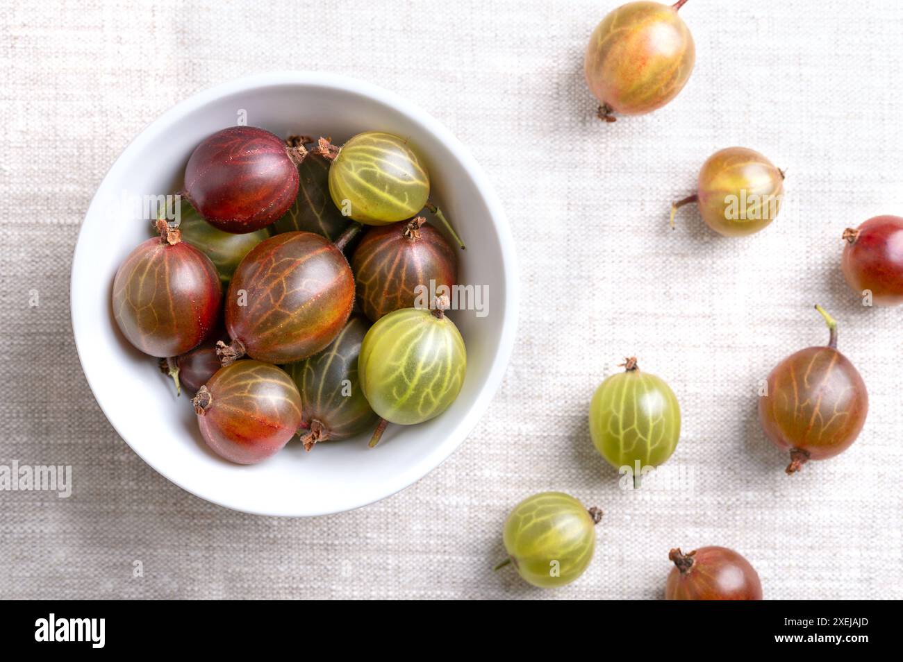 Green and red gooseberries in a white bowl on linen fabric. Fresh ripe ...